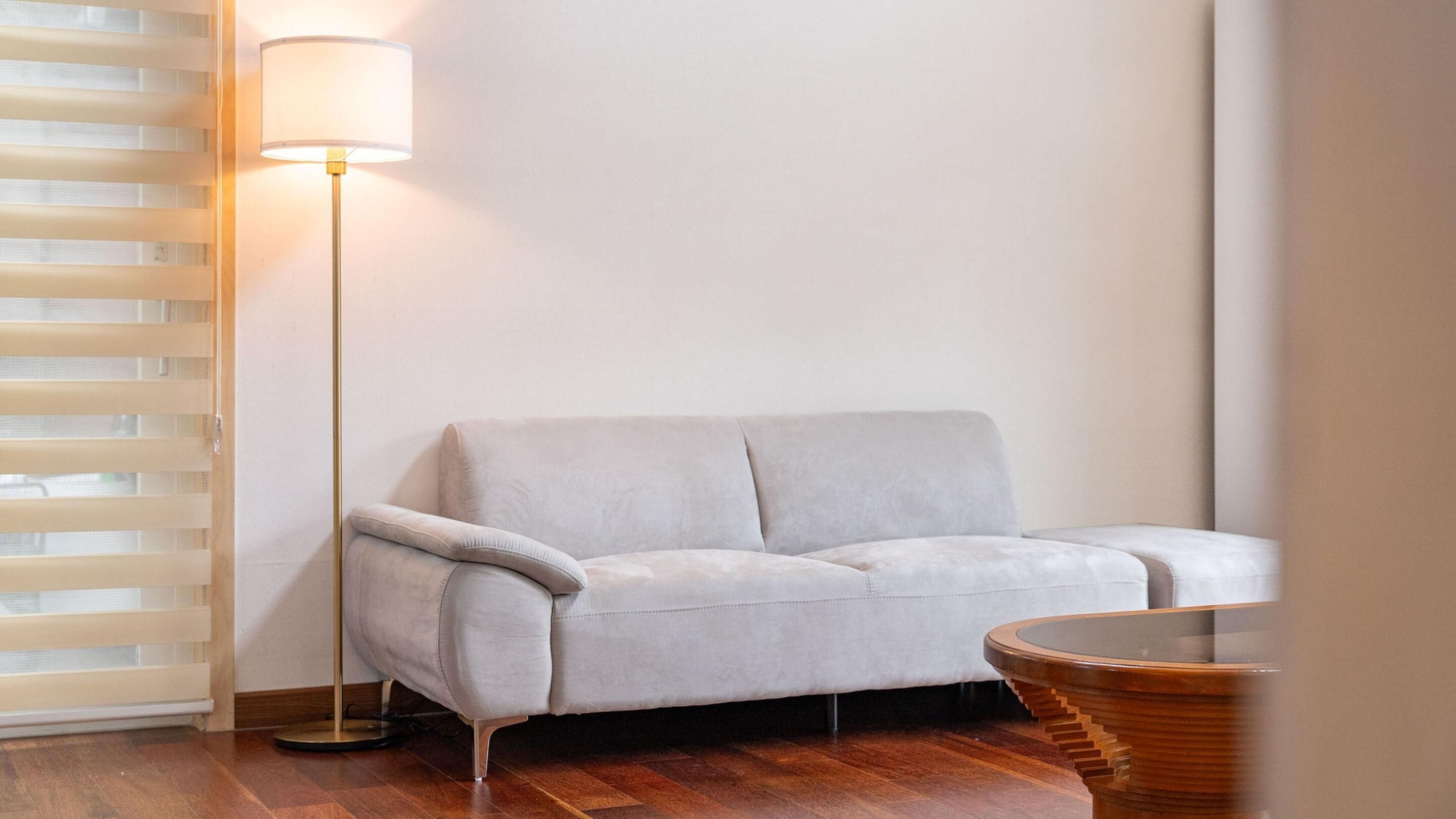 Uma sala de estar moderna com um sofá cinza claro, um abajur e uma mesa de centro redonda de madeira.