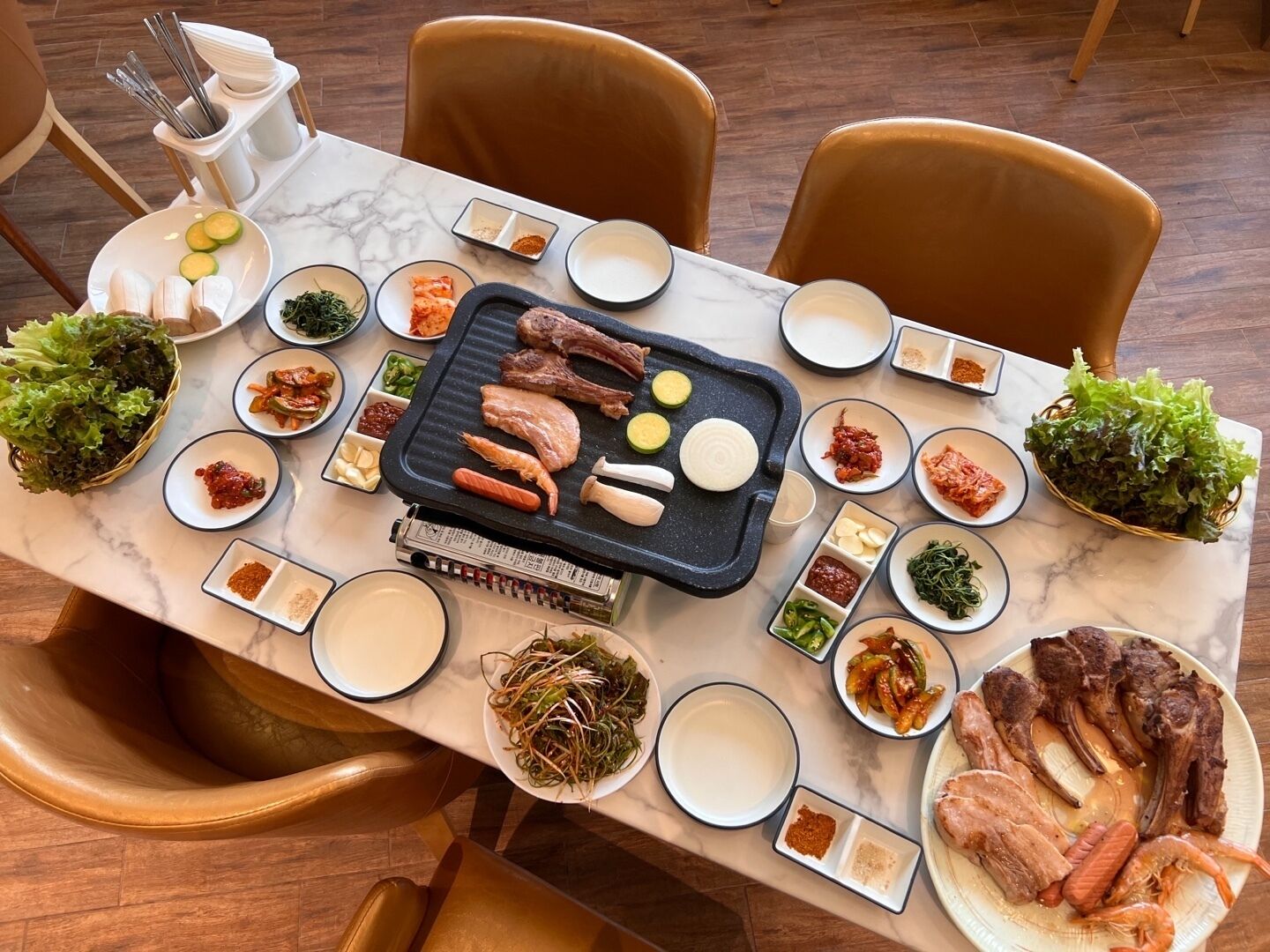 Mesa de jantar com diversos pratos, incluindo carnes grelhadas e legumes, dispostos para uma refeição.