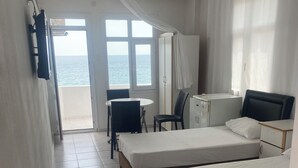 Quarto de hotel com duas camas, uma mesa pequena, uma cadeira, uma escrivaninha e vista para o mar.
