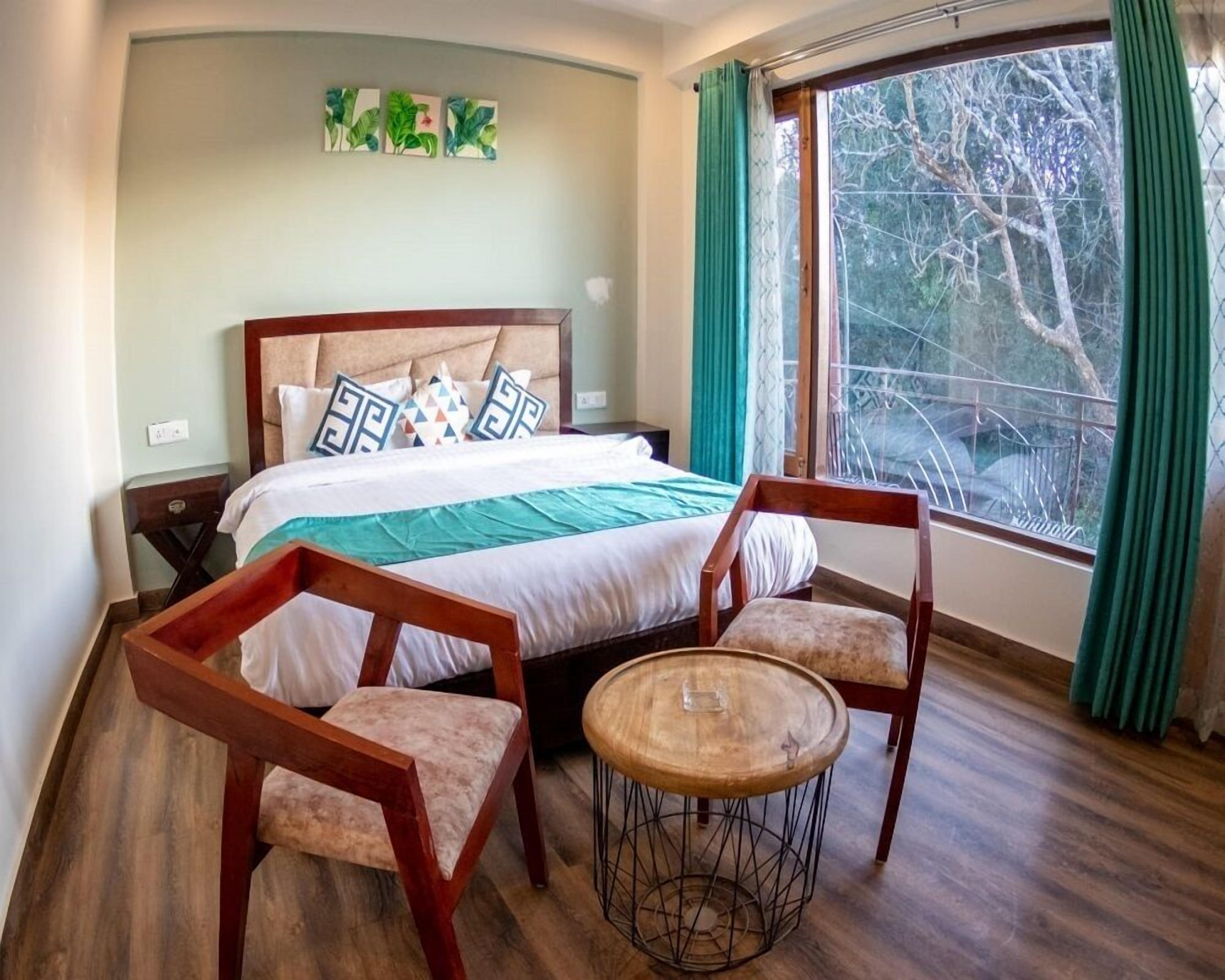 Um quarto com uma cama, duas cadeiras, uma mesa redonda pequena e uma janela com cortinas.