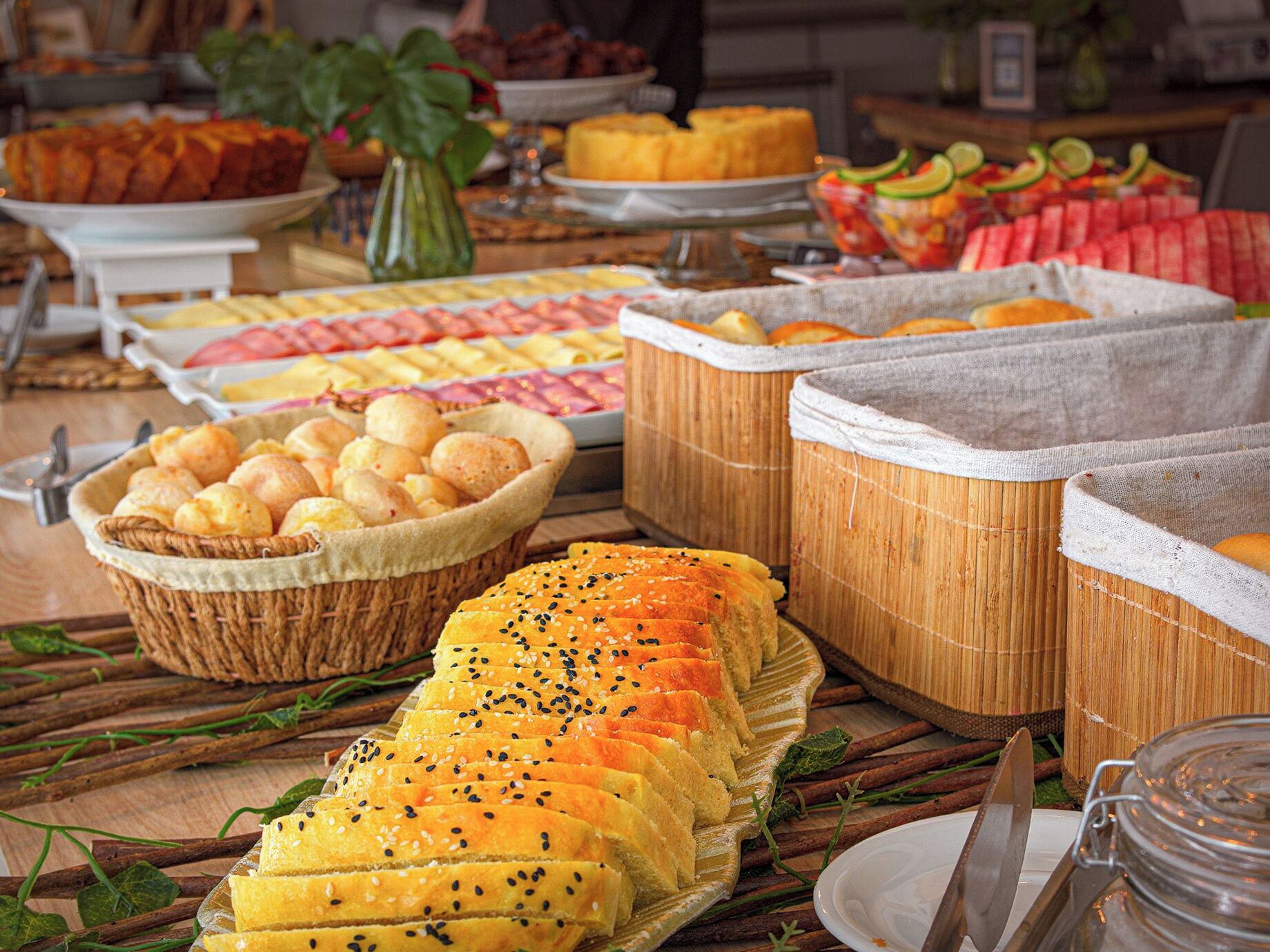 Buffet com diversos alimentos, incluindo pão, pastelaria e frutas.