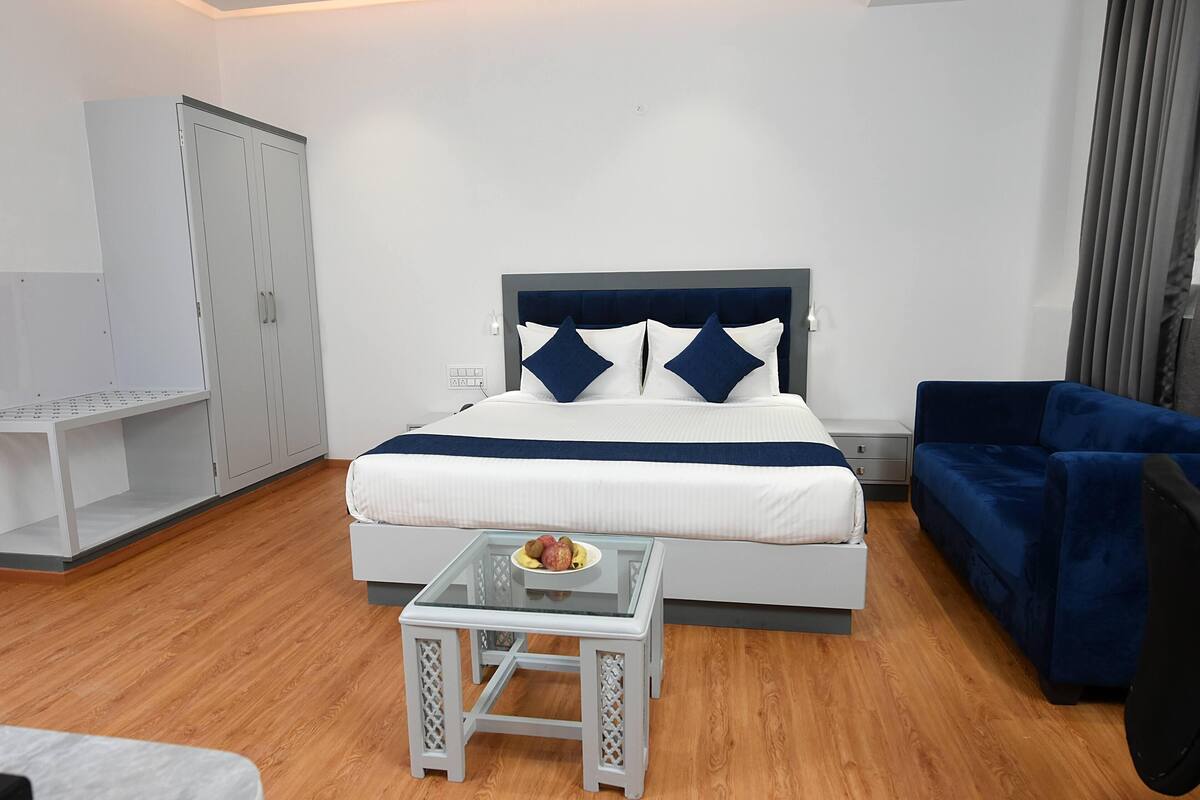 Quarto de hotel moderno com cama, uma pequena mesa com frutas, um sofá azul e um guarda-roupa.