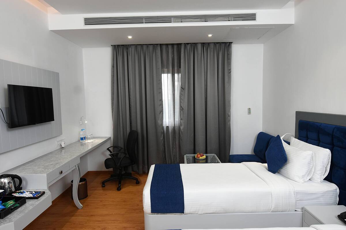 Quarto de hotel com cama, secretária, cadeira, televisão e janela com cortinas.