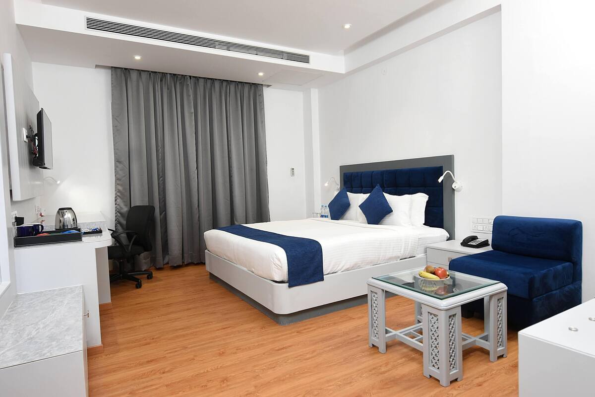 Quarto de hotel moderno com uma cama, uma mesa de escritório, uma cadeira e uma pequena mesa com frutas.