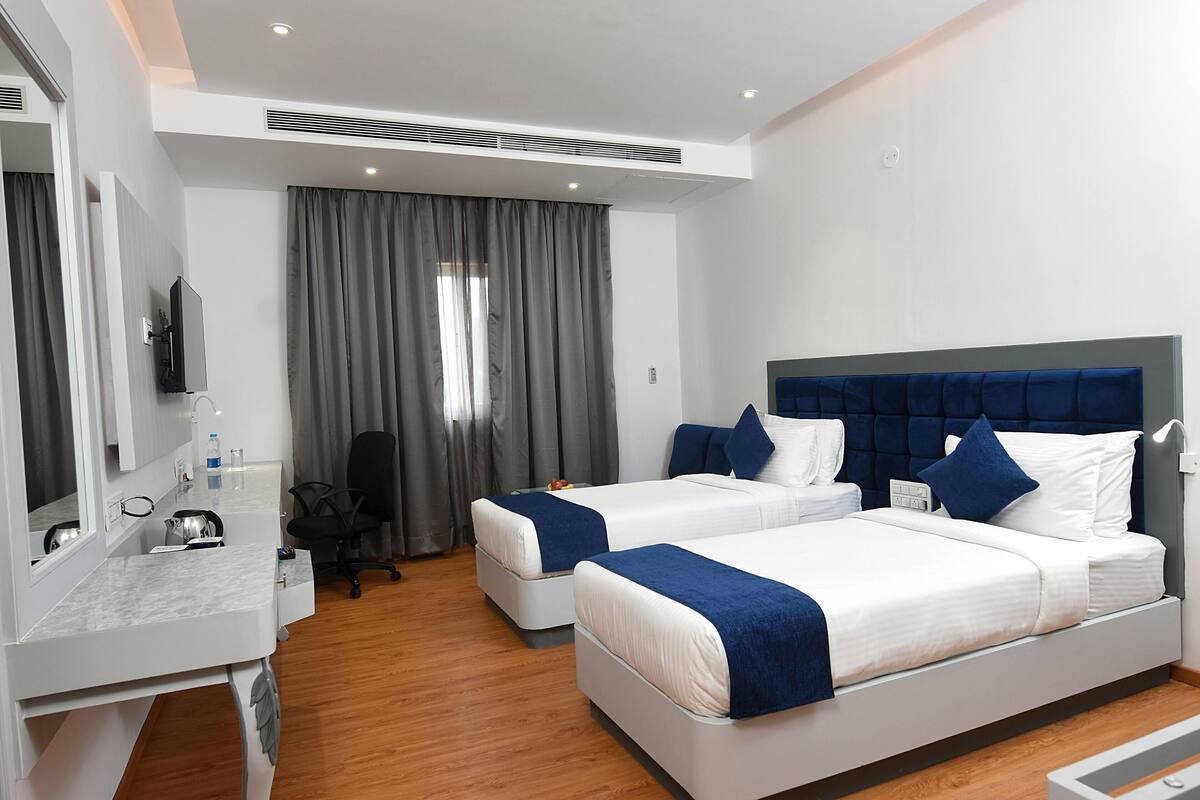 Quarto de hotel com duas camas, uma escrivaninha com espelho, uma cadeira e uma televisão.