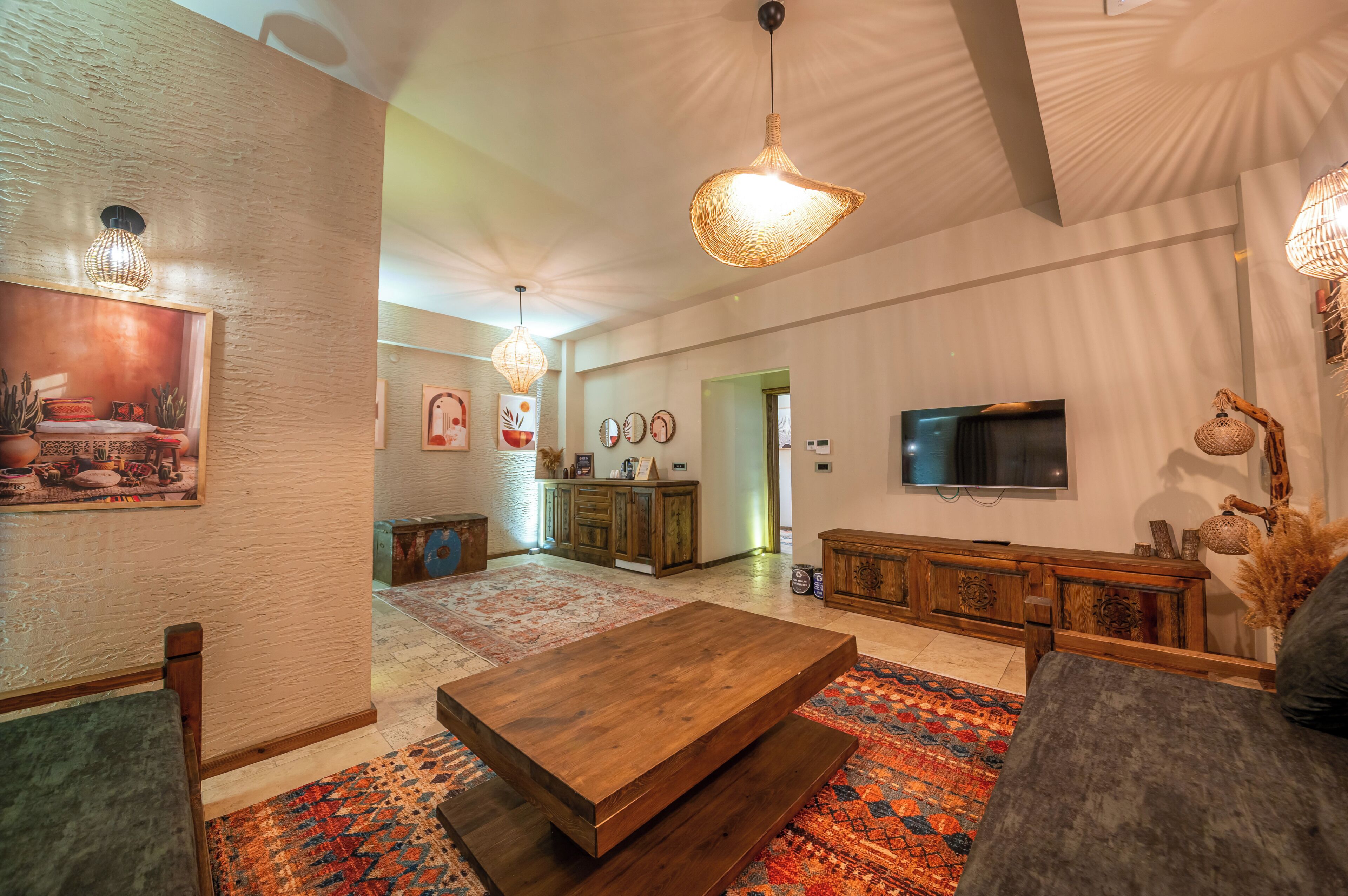 Uma sala de estar ampla com uma mesa de centro de madeira, uma televisão e um tapete estampado.
