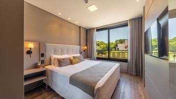 Quarto de hotel moderno com uma cama grande, mesas de cabeceira, uma varanda e vista para o verde através de amplas janelas.