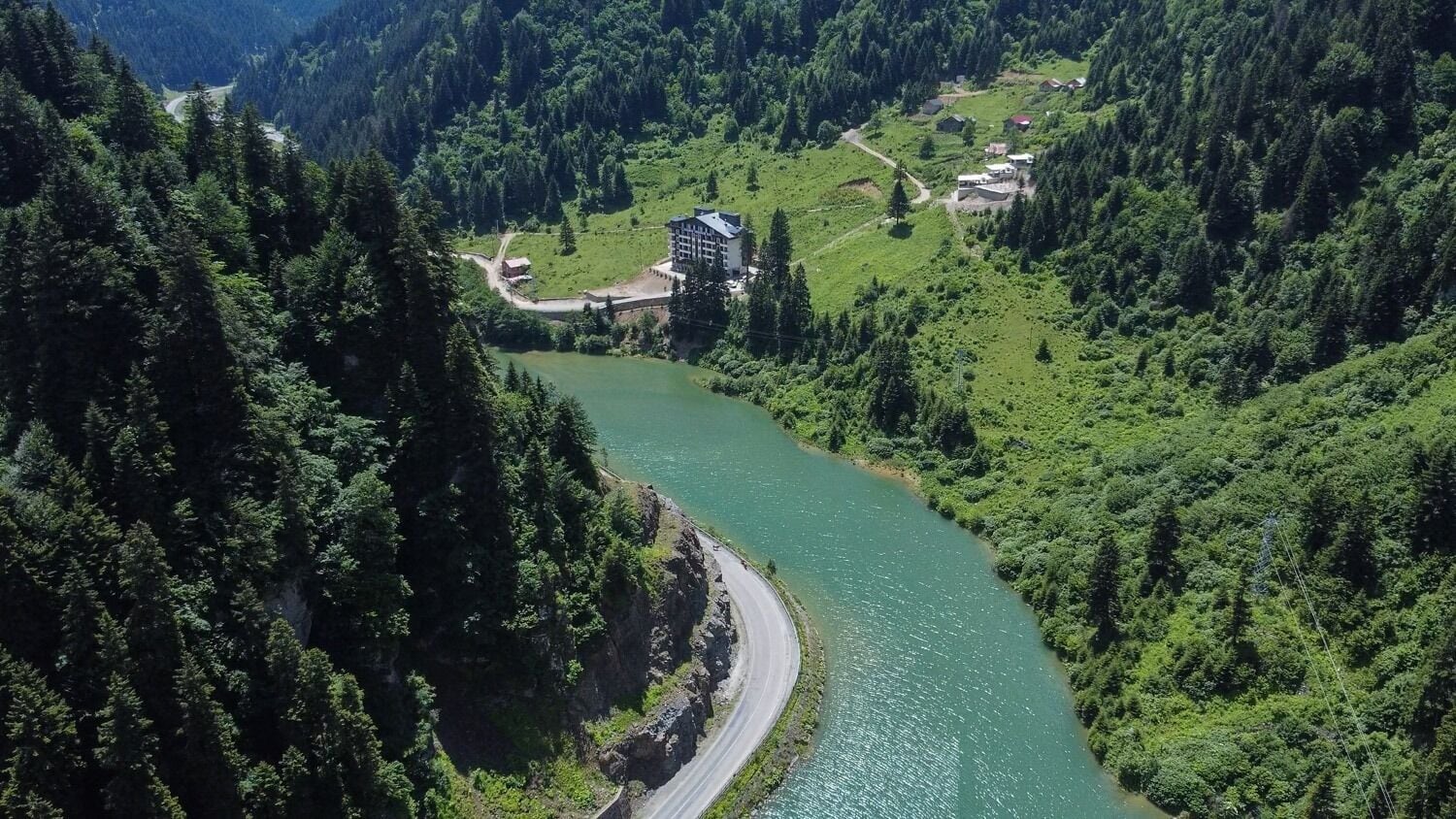 Paisagem montanhosa com um rio sinuoso, uma estrada e um complexo de edifícios com várias estruturas.