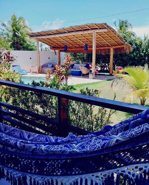 Uma área na piscina com espaço coberto para sentar, espreguiçadeiras e uma rede.