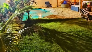 Área externa à noite com piscina, espreguiçadeiras e um espaço coberto para sentar.
