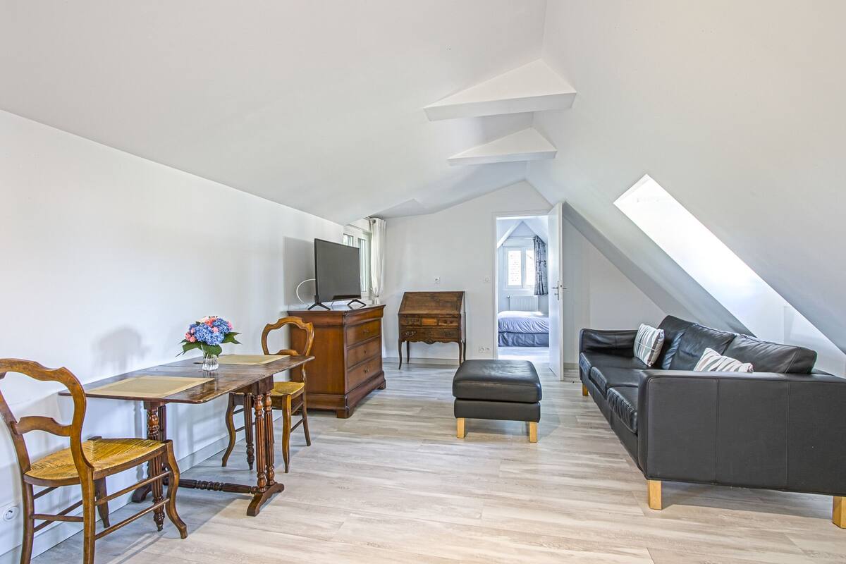 Quarto em estilo loft com área de jantar, sofá, televisão e escada para um andar superior.