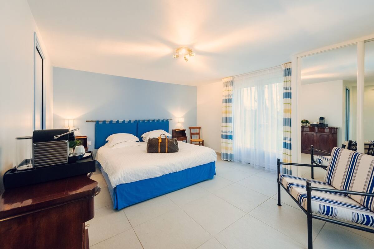 Quarto de hotel com cama, cadeira, escrivaninha e um espelho grande.