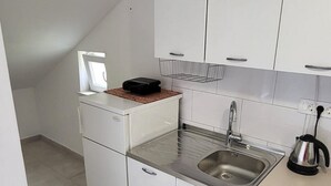 Uma kitchenette compacta com uma pia, chaleira e pequeno frigorífico.