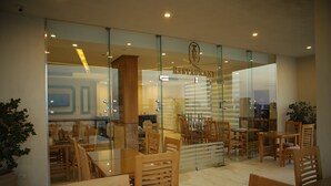 Restaurante com interior moderno, apresentando divisórias de vidro, mobiliário de madeira e um espaço limpo e bem iluminado.