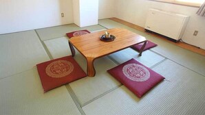 Quarto com piso de esteiras de tatame, uma mesa de madeira com bandeja e dois almofadas com padrão circular.