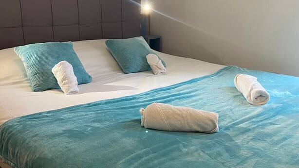 Cama bem arrumada com colcha e almofadas verde-água, cabeceira e uma obra de arte pendurada na parede.