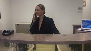 Uma mulher no balcão de recepção de um hotel, com um laptop e um telefone.