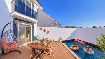Uma área de piscina moderna ao ar livre com um deck de madeira, uma cadeira suspensa e uma mesa posta para refeições.