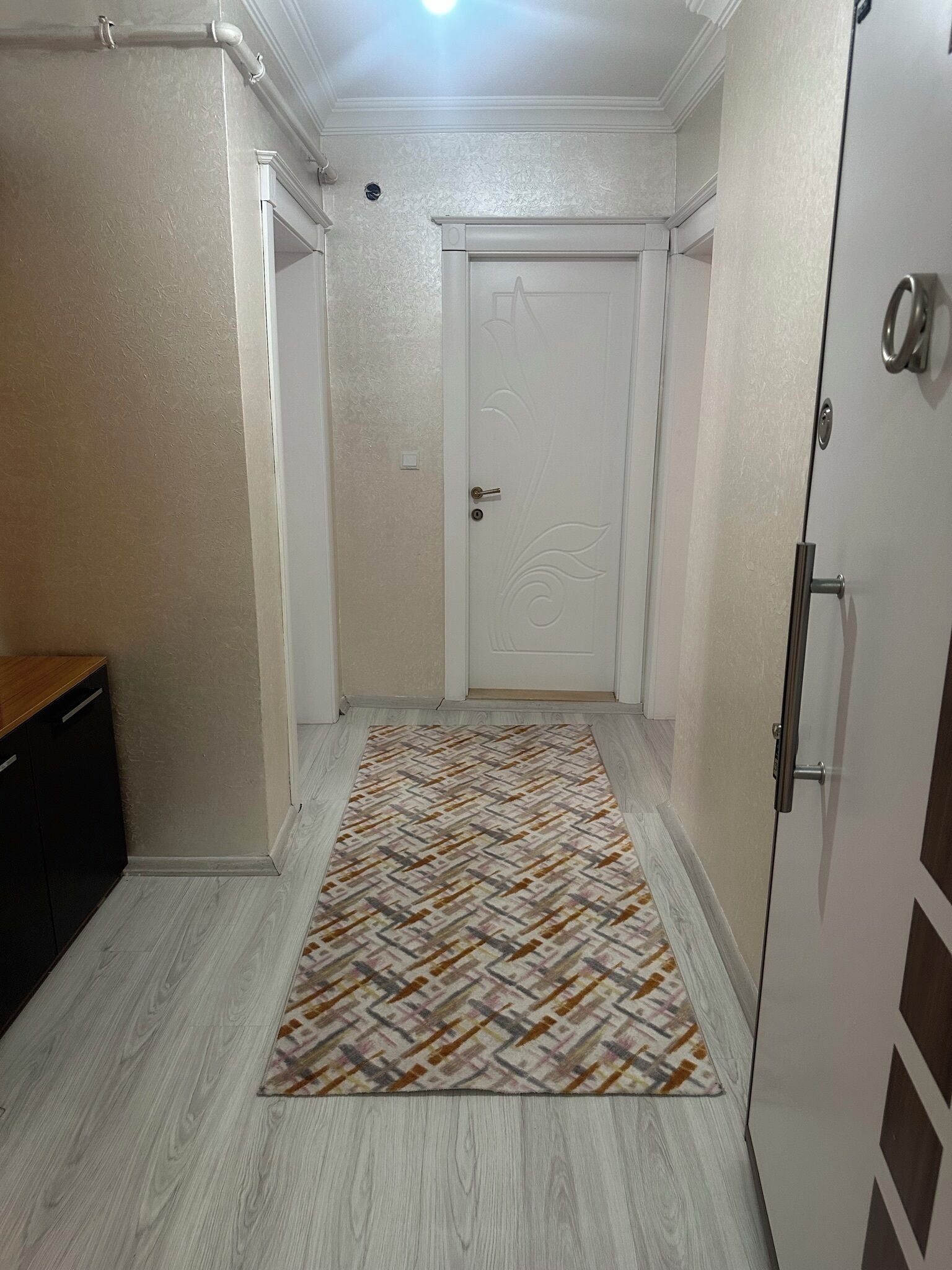 Um corredor com tapete estampado, porta branca e guarda-roupa.