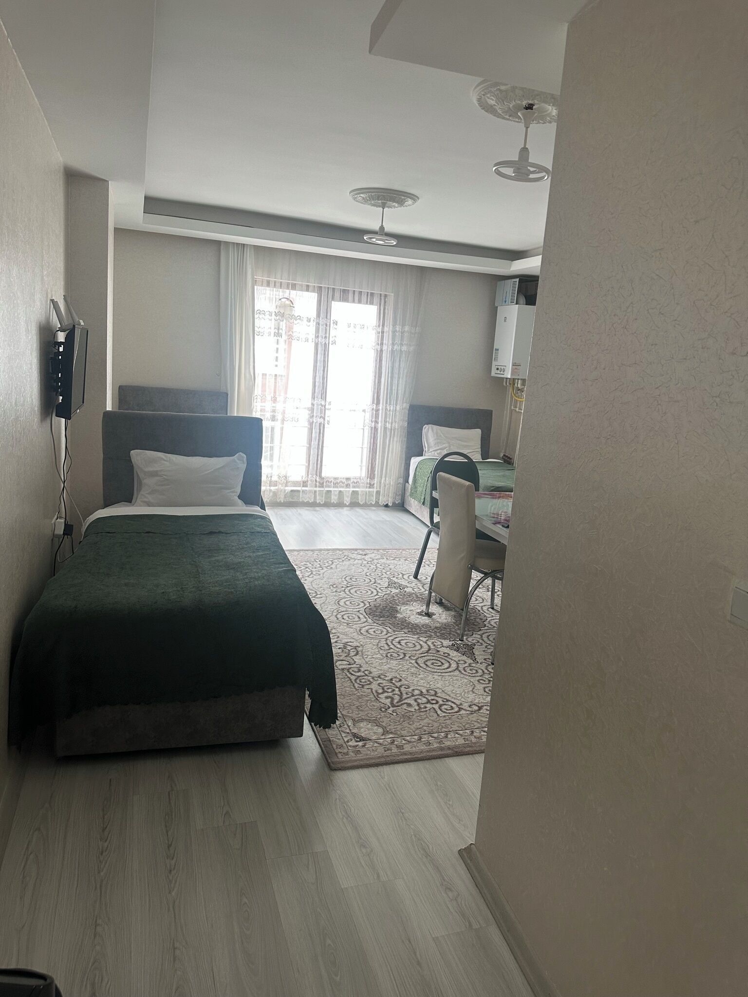 Quarto de hotel com cama, mesa, cadeira, televisão e ventoinha no teto.