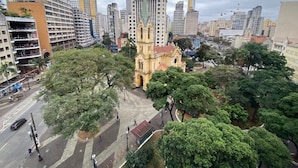 Paisagem urbana com uma igreja amarela imponente e uma torre verde, cercada por árvores e edifícios modernos.