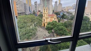 Vista da janela mostrando um horizonte urbano com uma igreja amarela destacada e edifícios modernos ao redor.