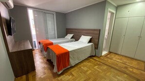 Quarto de hotel com duas camas, piso de madeira, um guarda-roupa e uma televisão.