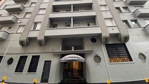 Um hotel moderno com fachada simétrica, várias varandas e uma entrada central com guarda-sol.
