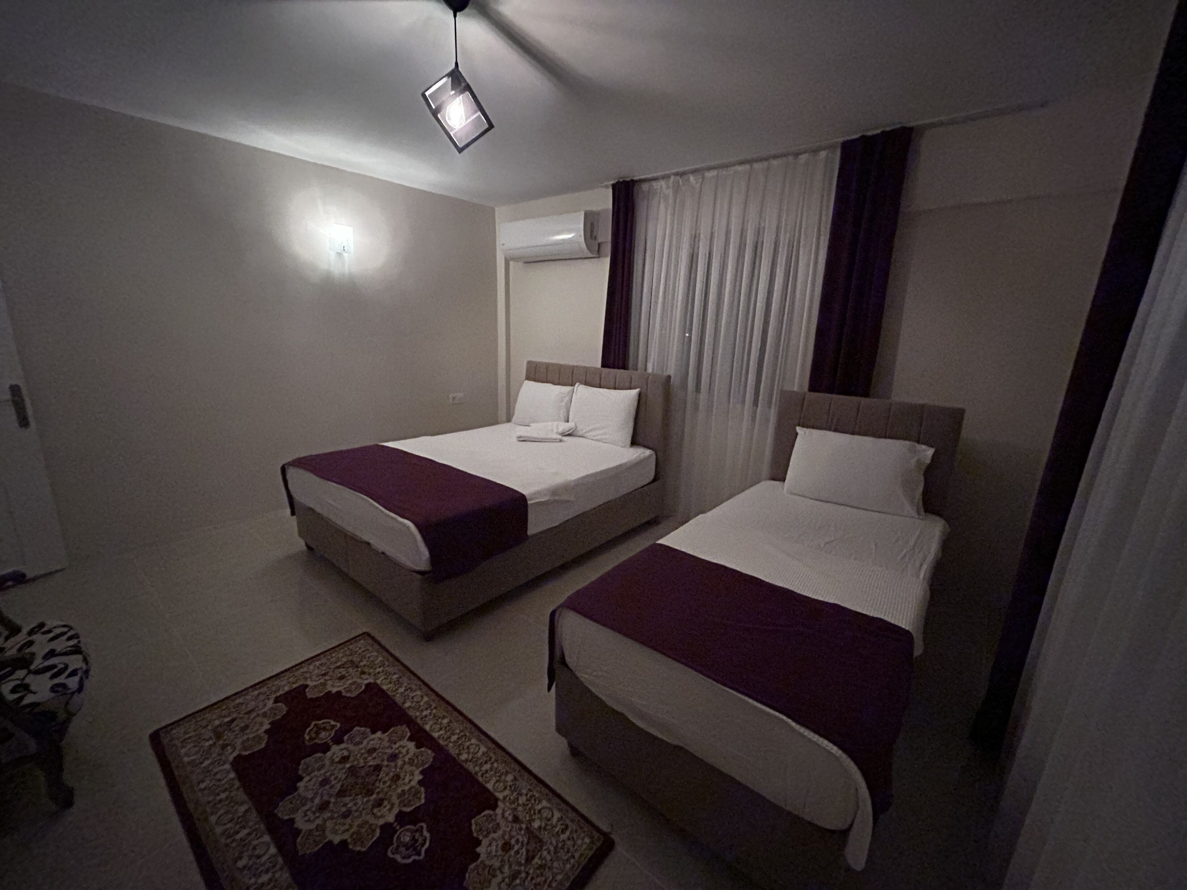 Quarto de hotel com duas camas de solteiro, um pequeno espaço de estar e uma janela com cortinas.