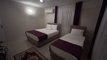 Quarto de hotel com duas camas de solteiro, um pequeno espaço de estar e uma janela com cortinas.