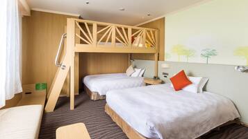 Quarto de hotel com duas camas, uma cama beliche, uma pequena escrivaninha e uma mesa de cabeceira.