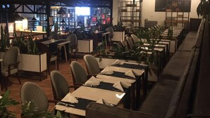 Um restaurante com mesas compridas e cabines, plantas em vasos e teto alto com vigas aparentes.