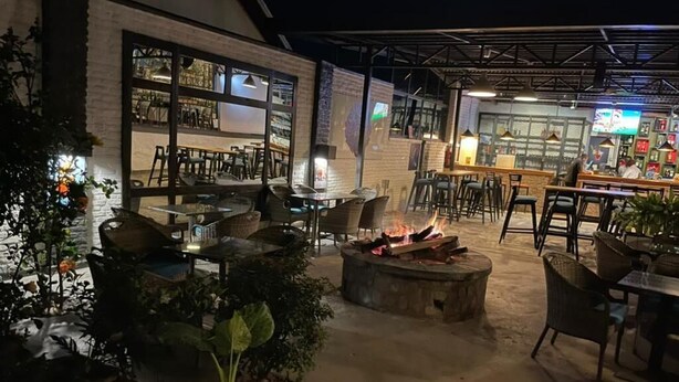 Uma área externa com mesas, cadeiras, lareira e plantas em vasos.