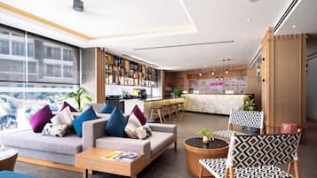 Uma sala de estar moderna com um sofá, mesa de centro e cadeira estampada. Uma cozinha com balcão é visível ao fundo.