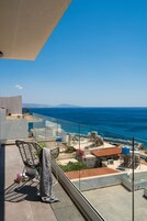 Uma varanda com vista para o mar, uma cadeira e uma mesa pequena.