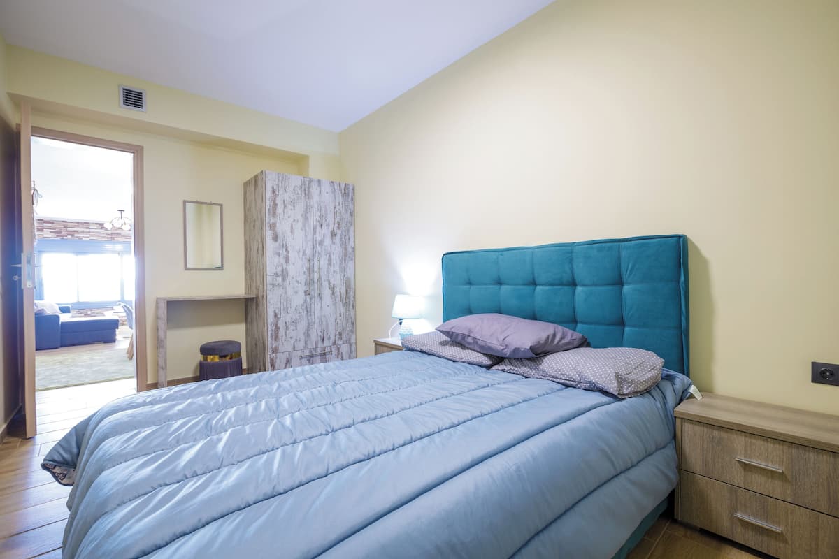 Quarto com cama, mesas de cabeceira, um armário de madeira e vista para o exterior.
