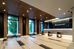 Um lobby de hotel moderno com balcão de recepção, área de estar e amplas janelas com vista para o verde.
