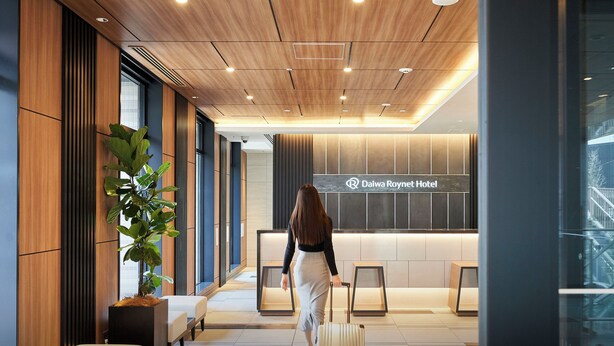 Um lobby moderno de hotel com balcão de recepção, área de estar e uma grande planta em vaso.