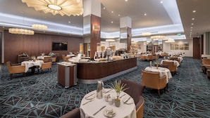 Um espaço de refeições de hotel com mesas redondas, cadeiras e um balcão de buffet.