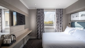 Quarto de hotel moderno com uma cama grande, televisão de tela plana, cafeteira e vista para a cidade.