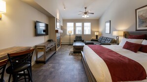 Quarto de hotel com cama, escrivaninha, cadeira, televisão e ventoinha no teto.
