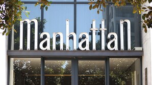 Um edifício com grandes letras brancas e arqueadas formando a palavra 'Manhattan' sobre a entrada.