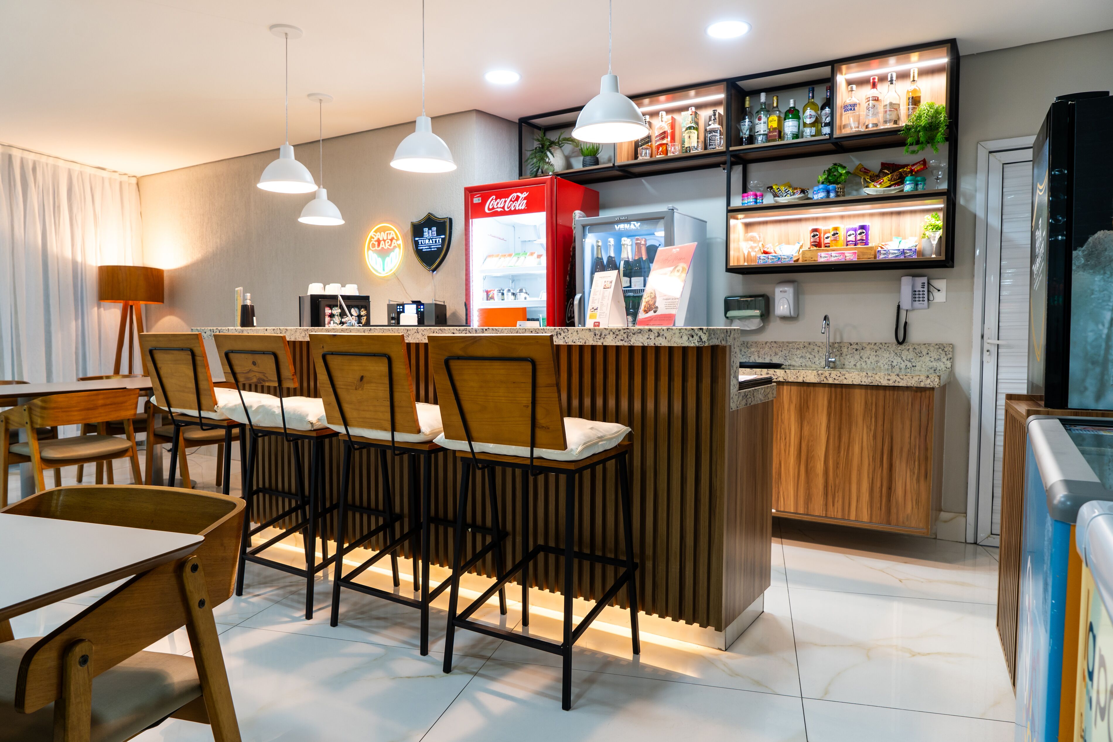 Uma área de bar moderna com banquetas de madeira, um frigorífico, prateleiras com garrafas e um balcão.