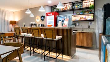 Uma área de bar moderna com banquetas de madeira, um frigorífico, prateleiras com garrafas e um balcão.