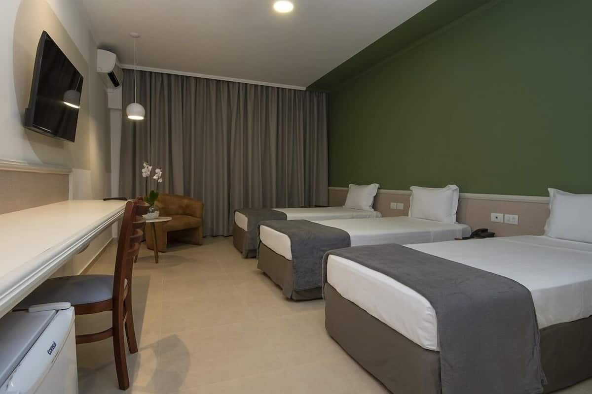 Quarto de hotel com escrivaninha, duas camas, uma cadeira, televisão e cortina.