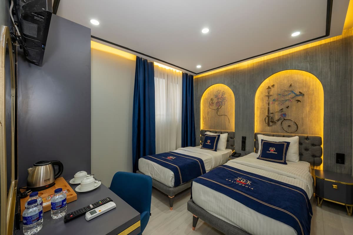 Quarto de hotel com duas camas, uma escrivaninha com chaleira, duas garrafas de água, um controle remoto e uma mesa de cabeceira.
