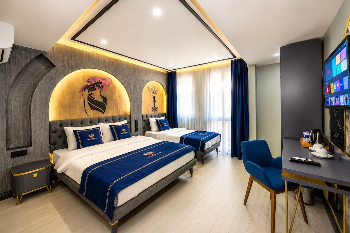 Quarto de hotel com duas camas, uma escrivaninha com cadeira, televisão e minibar.