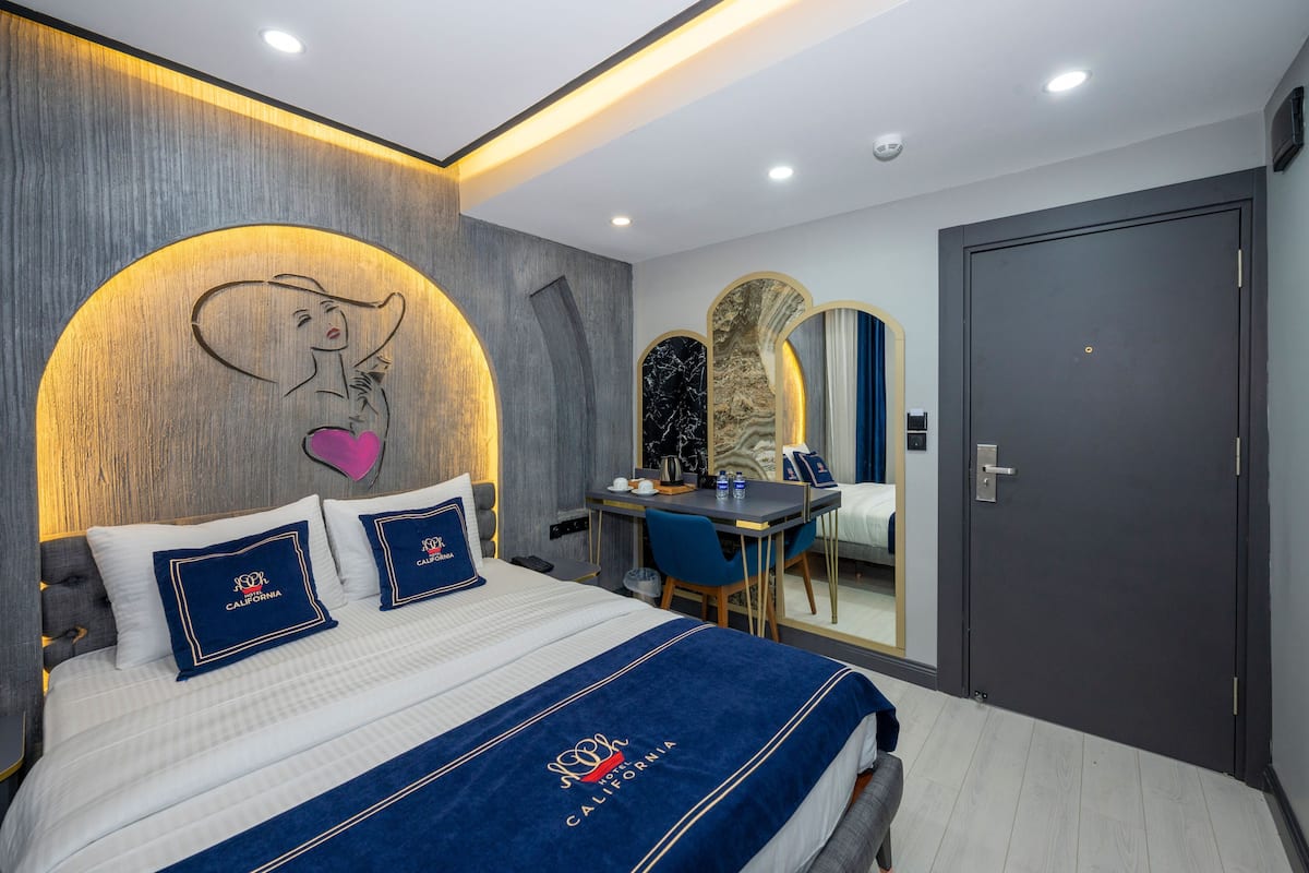 Quarto de hotel com cama, escrivaninha, espelho e porta.
