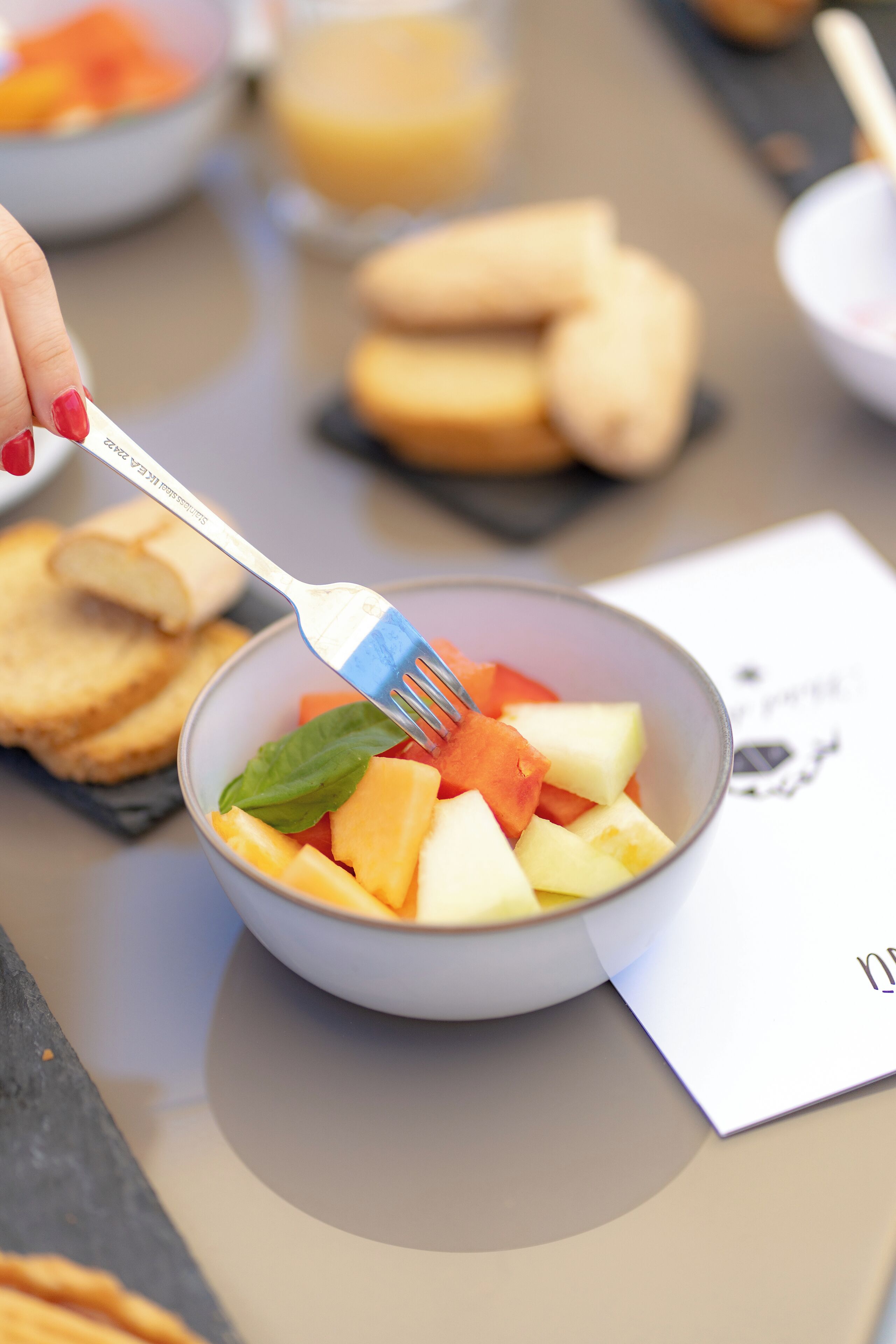 Uma saladeira com salada de frutas, um garfo, pão e um guardanapo sobre a mesa.