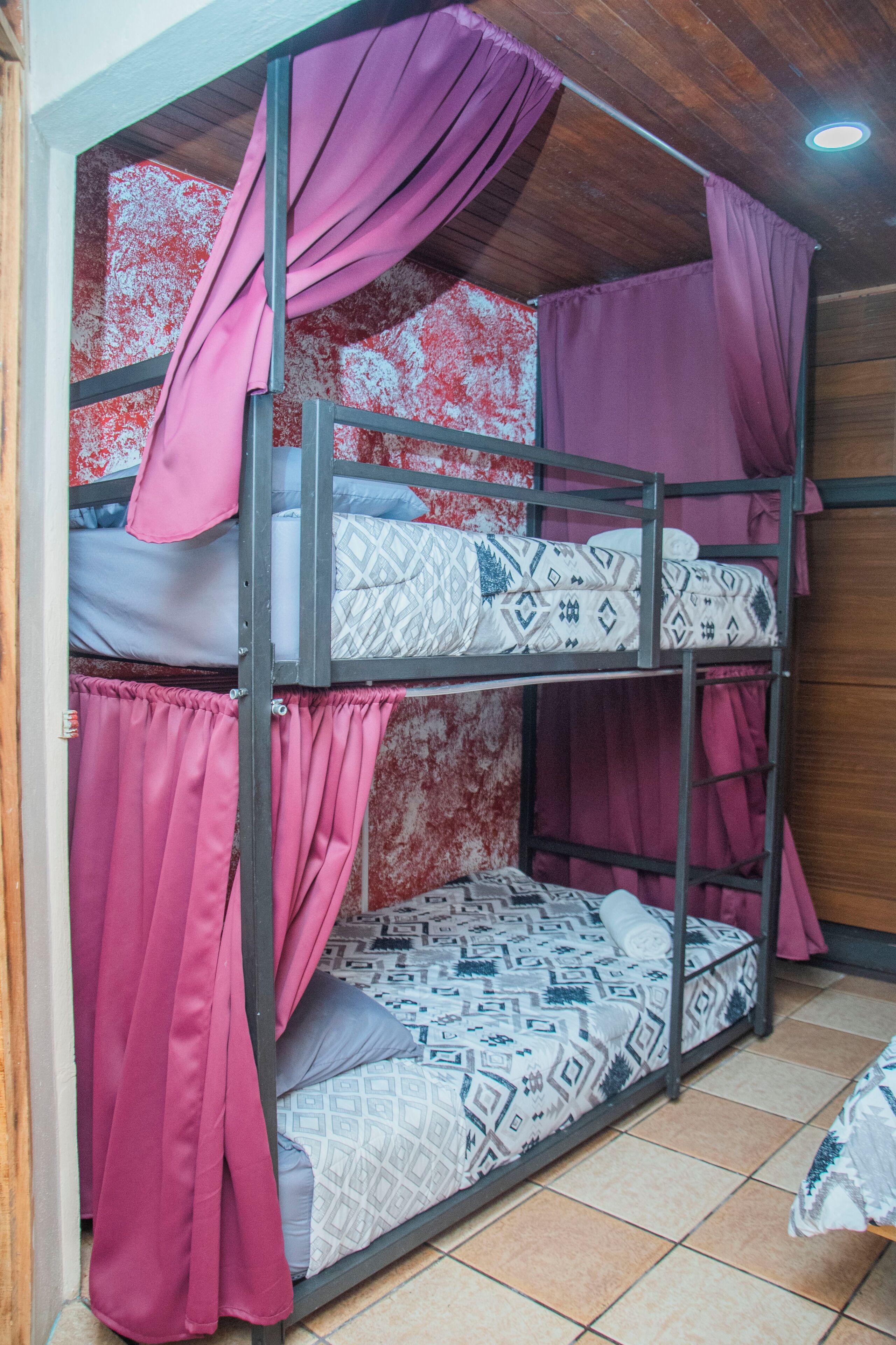 Uma cama beliche com cortinas cor-de-rosa, roupa de cama estampada e teto de madeira.
